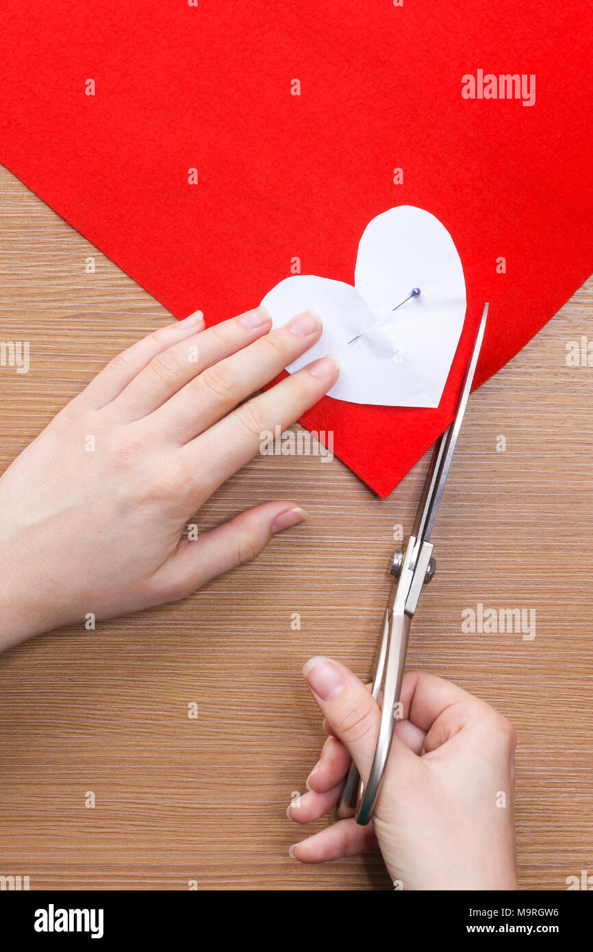 top view of hands cutting heart pattern from felt fabric. sewing tools ...