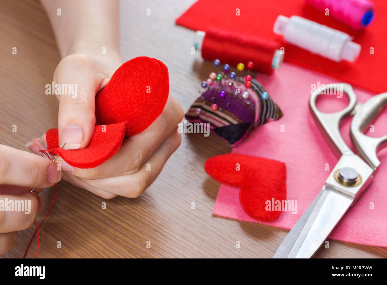 close up view of hands sewing heart pattern cut from red fabric. sewing ...