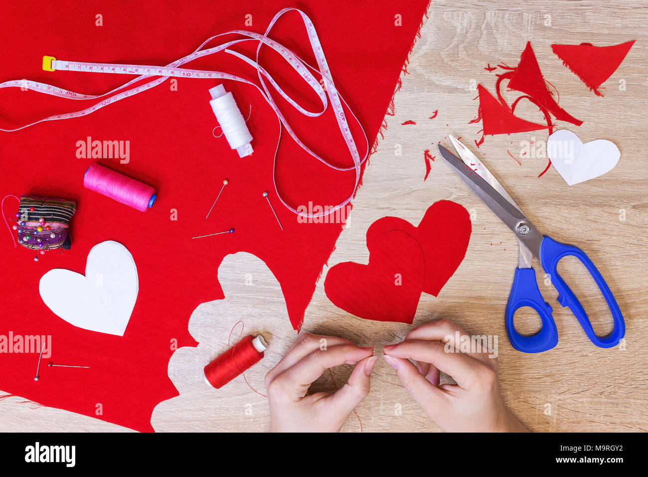 top view of hands sewing heart pattern cut from red fabric. sewing ...