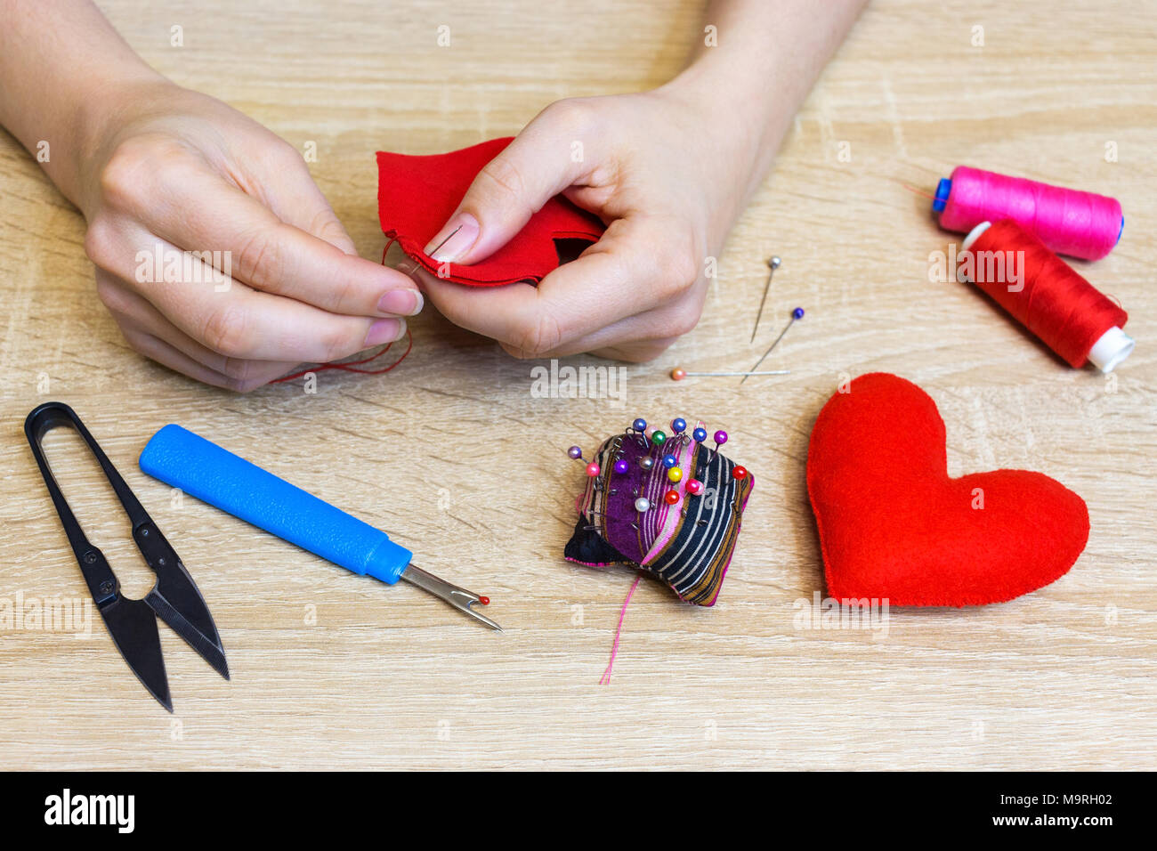 close up view of hands sewing heart pattern cut from red fabric. sewing ...