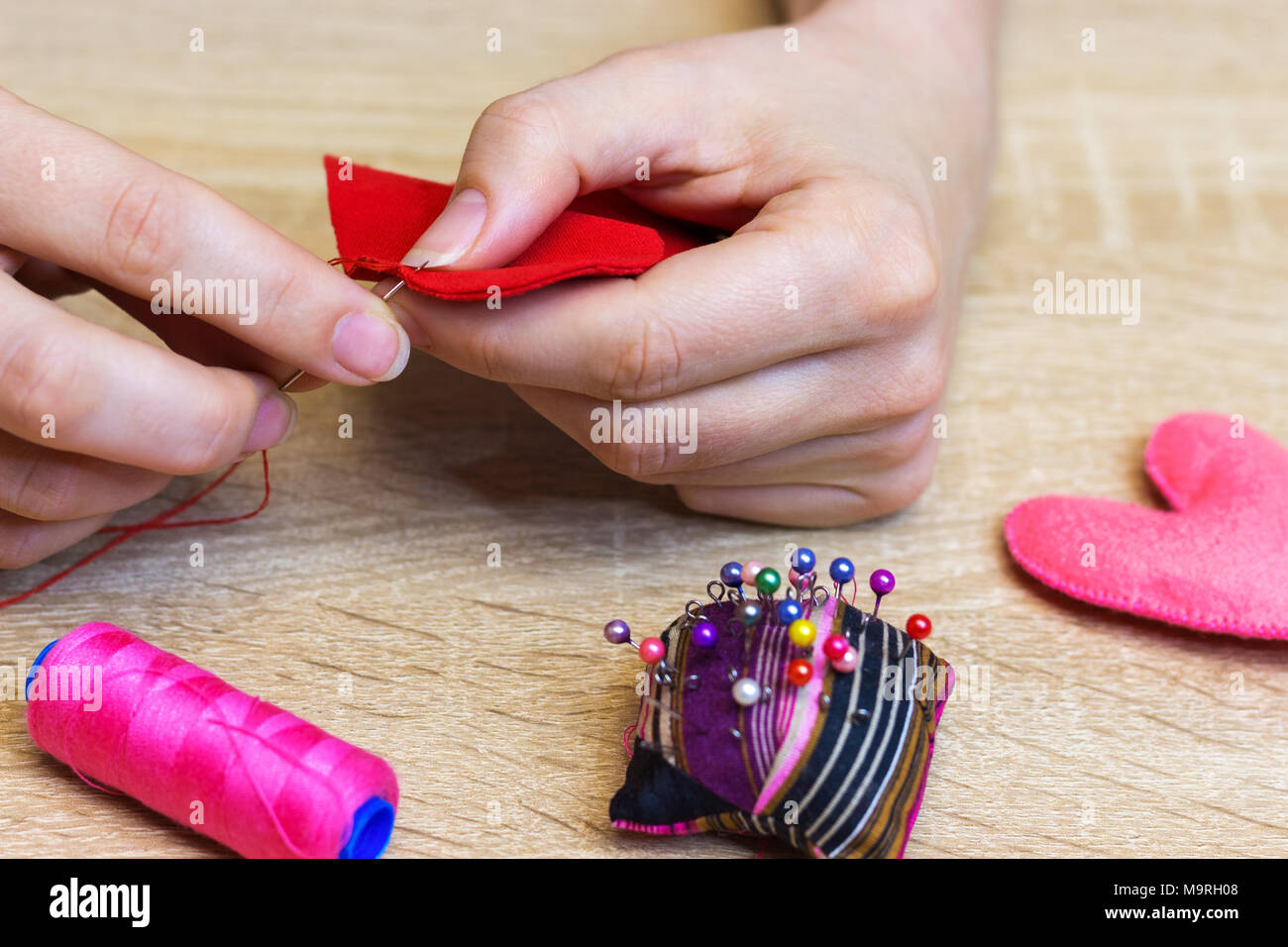 close up view of hands sewing heart pattern cut from red fabric. sewing ...