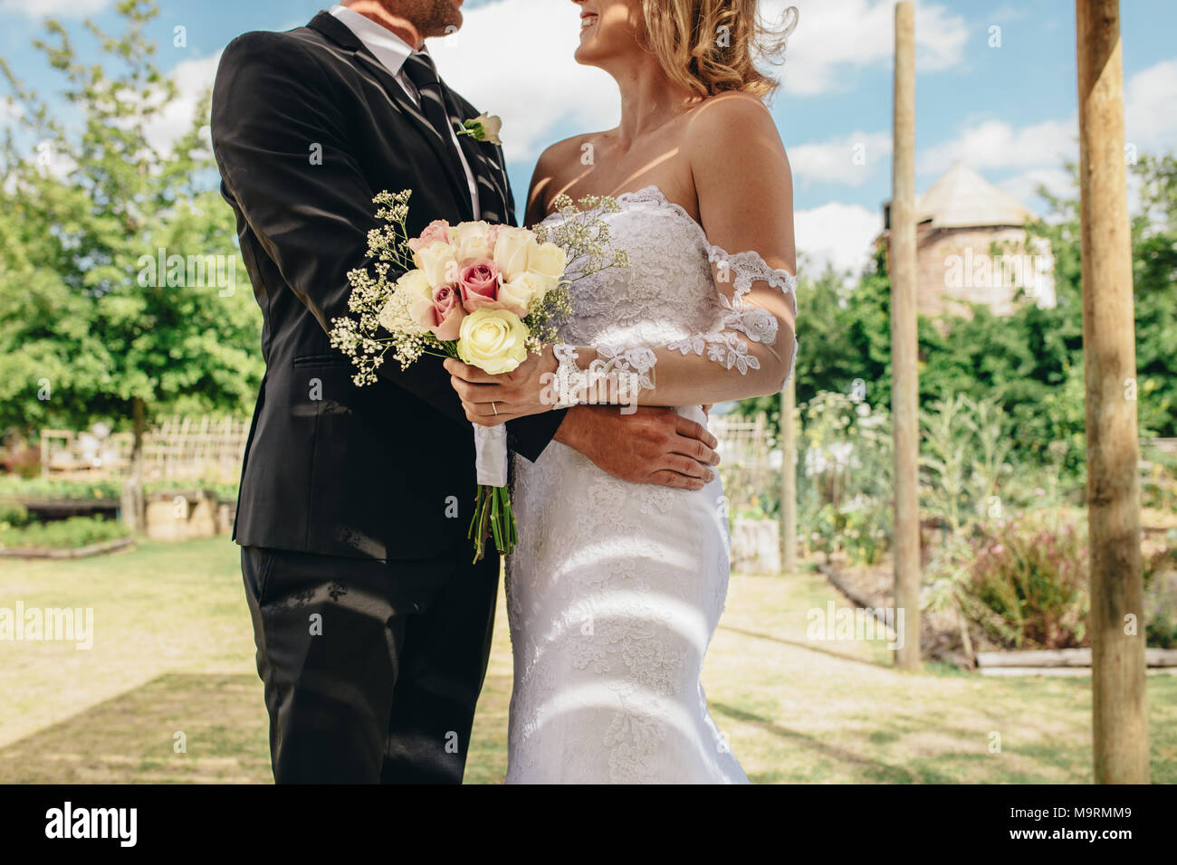 Bride and groom standing together with a flower bouquet on their ...