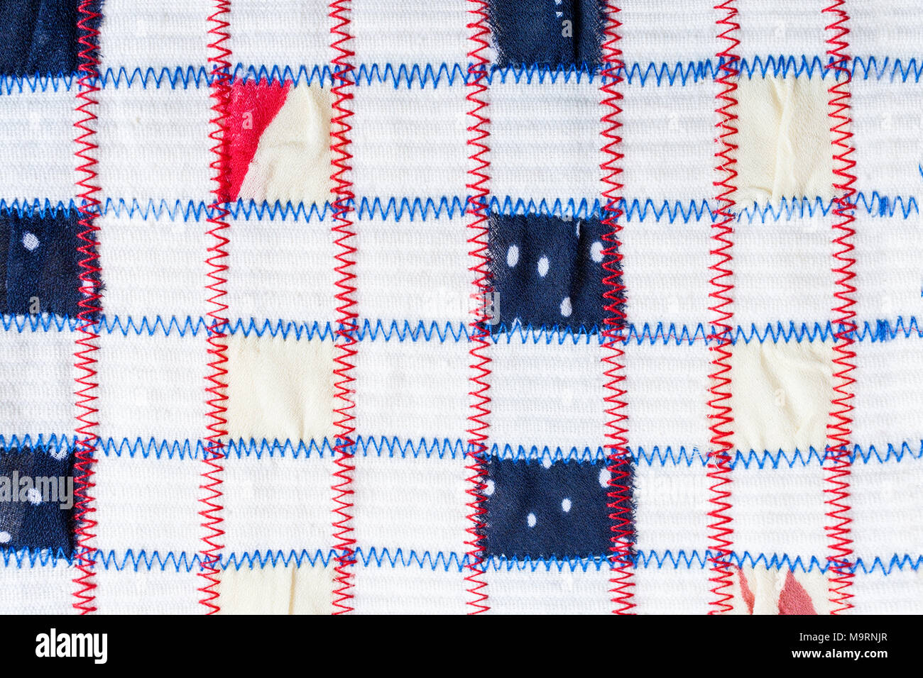 Textile pattern of square pieces of colored fabrics, sewn by red and blue zigzag seams on white ...