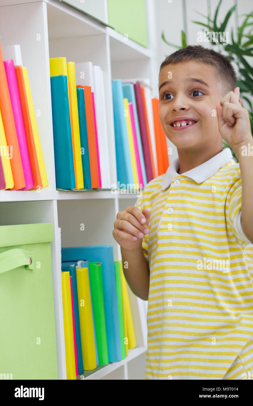little boy standing next to a bookcase in the library Stock Photo - Alamy