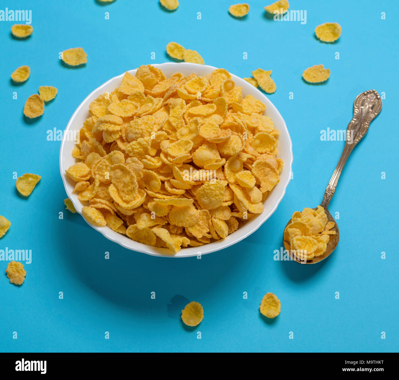 cornflakes in a white ceramic plate and an iron spoon on a blue ...