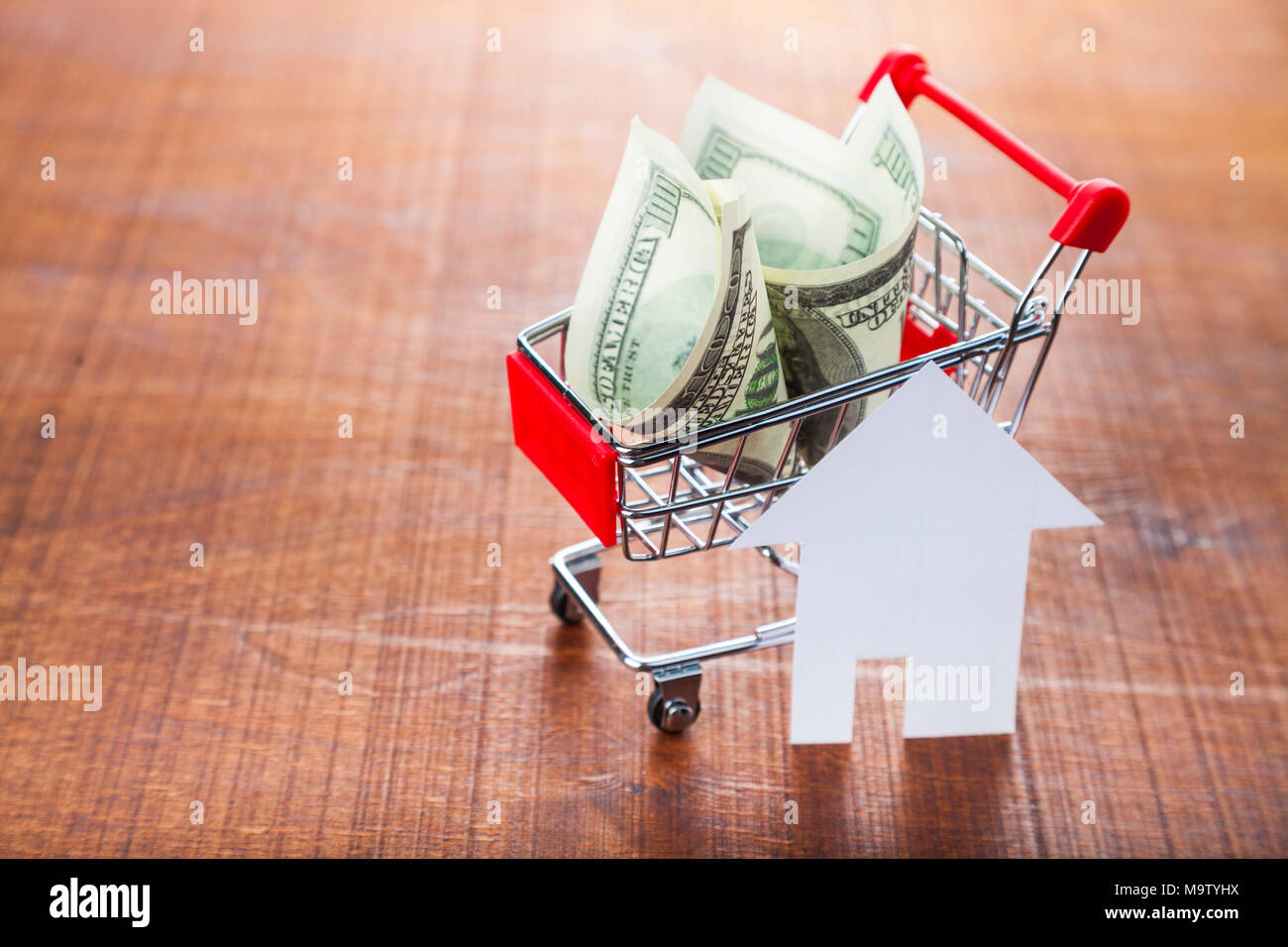 Money in a shop trolley and a house on a wooden background.. Buying a ...