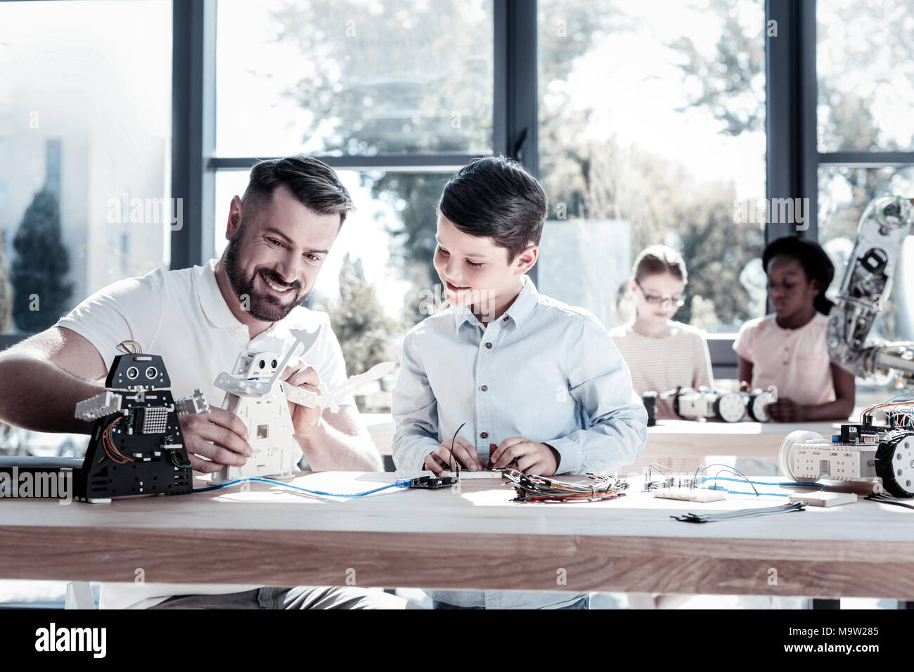 Joyful teacher and student smiling while working on robotic machine ...