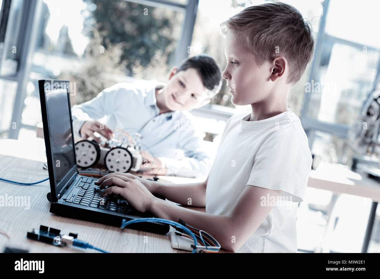 Intelligent schoolchildren working on laptop after constructing robot ...