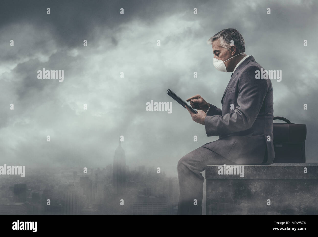 Businessman sitting on a rooftop in a polluted city and using a tablet ...