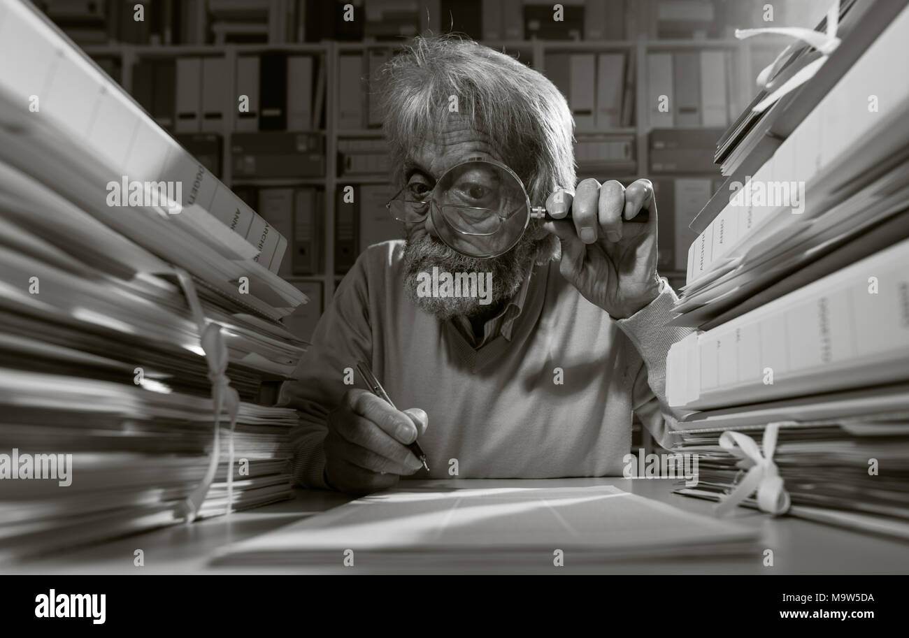 Senior researcher using a magnifying glass and writing, he is ...