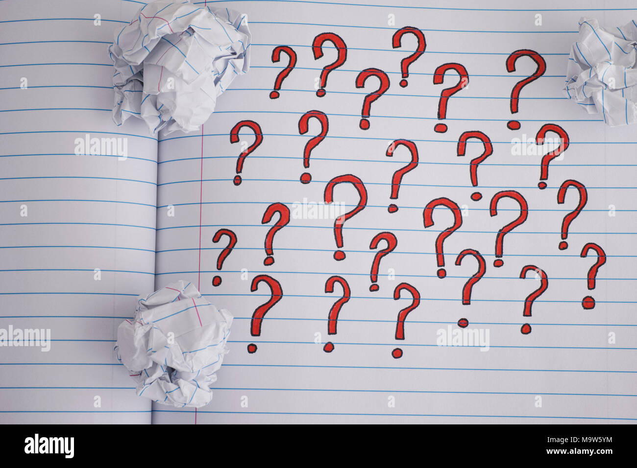 Question marks on notebook sheet with some crumpled paper balls on it ...