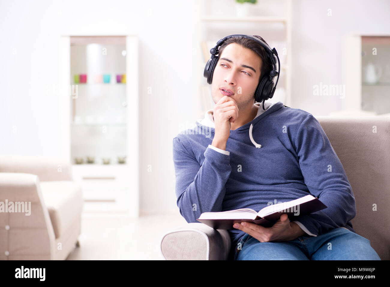 Young man reading book and listening to audio book Stock Photo - Alamy