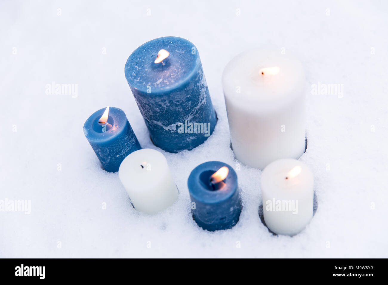 Blue and white candles flaming on snow Stock Photo - Alamy