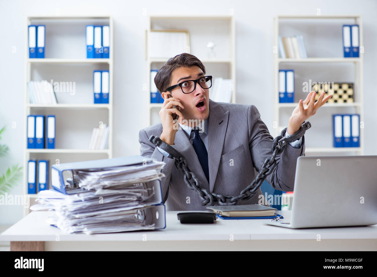 Busy employee chained to his office desk Stock Photo - Alamy
