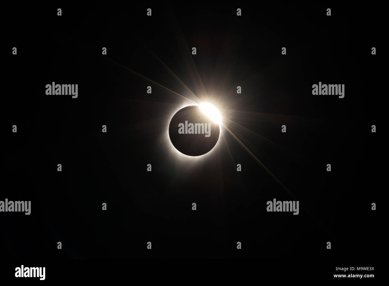 Solar eclipse just after totality with the sun flaring out from behind the moon as viewed from ...