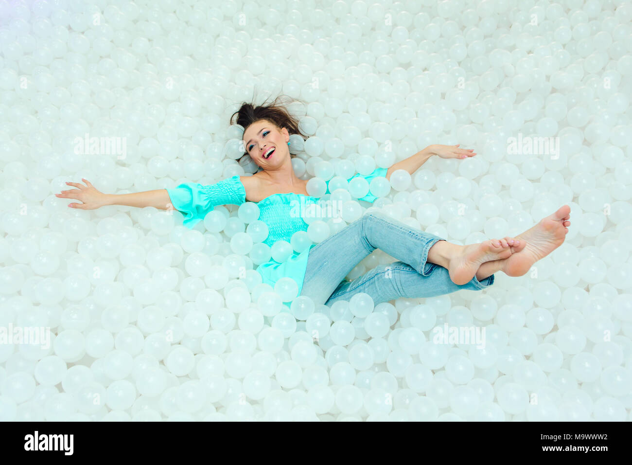 Happy beautiful woman lays surrounded by white plastic balls in the dry ...