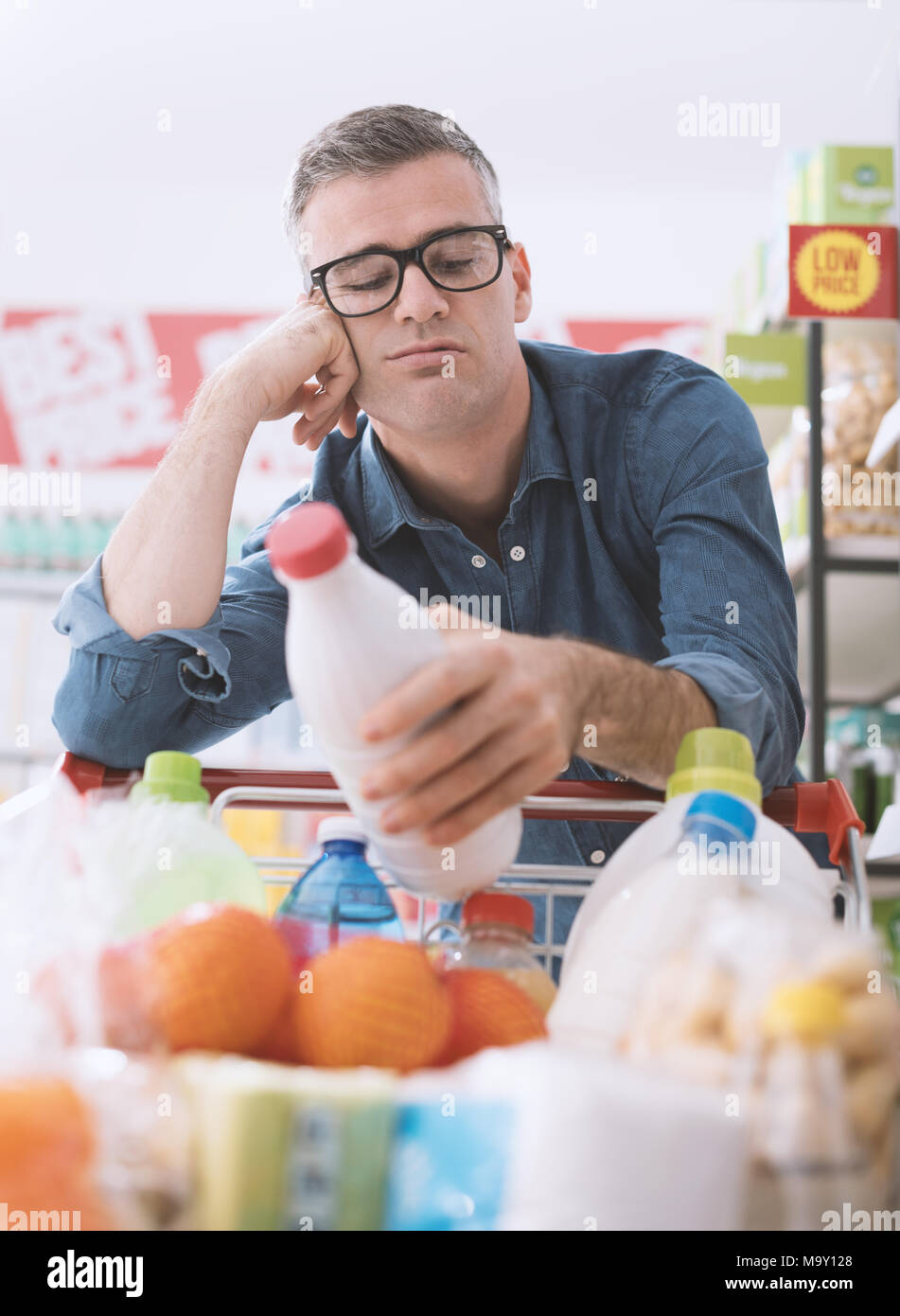 Sad tired man doing grocery shopping at the supermarket, he is leaning ...