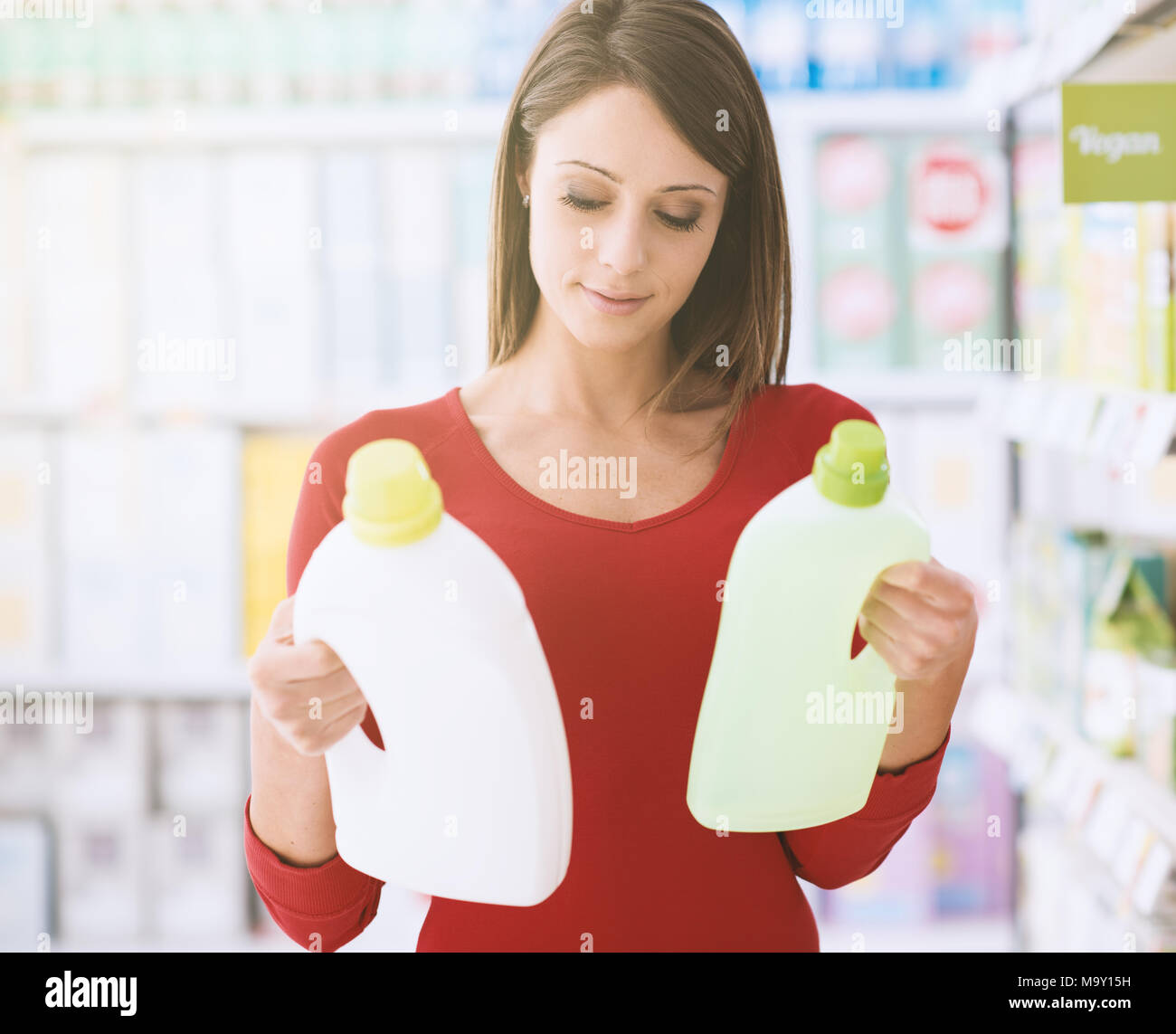 Woman shopping at the supermarket and comparing detergent products, she ...