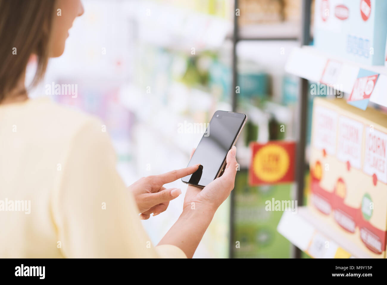 Woman doing grocery shopping at the supermarket and using a smart phone ...