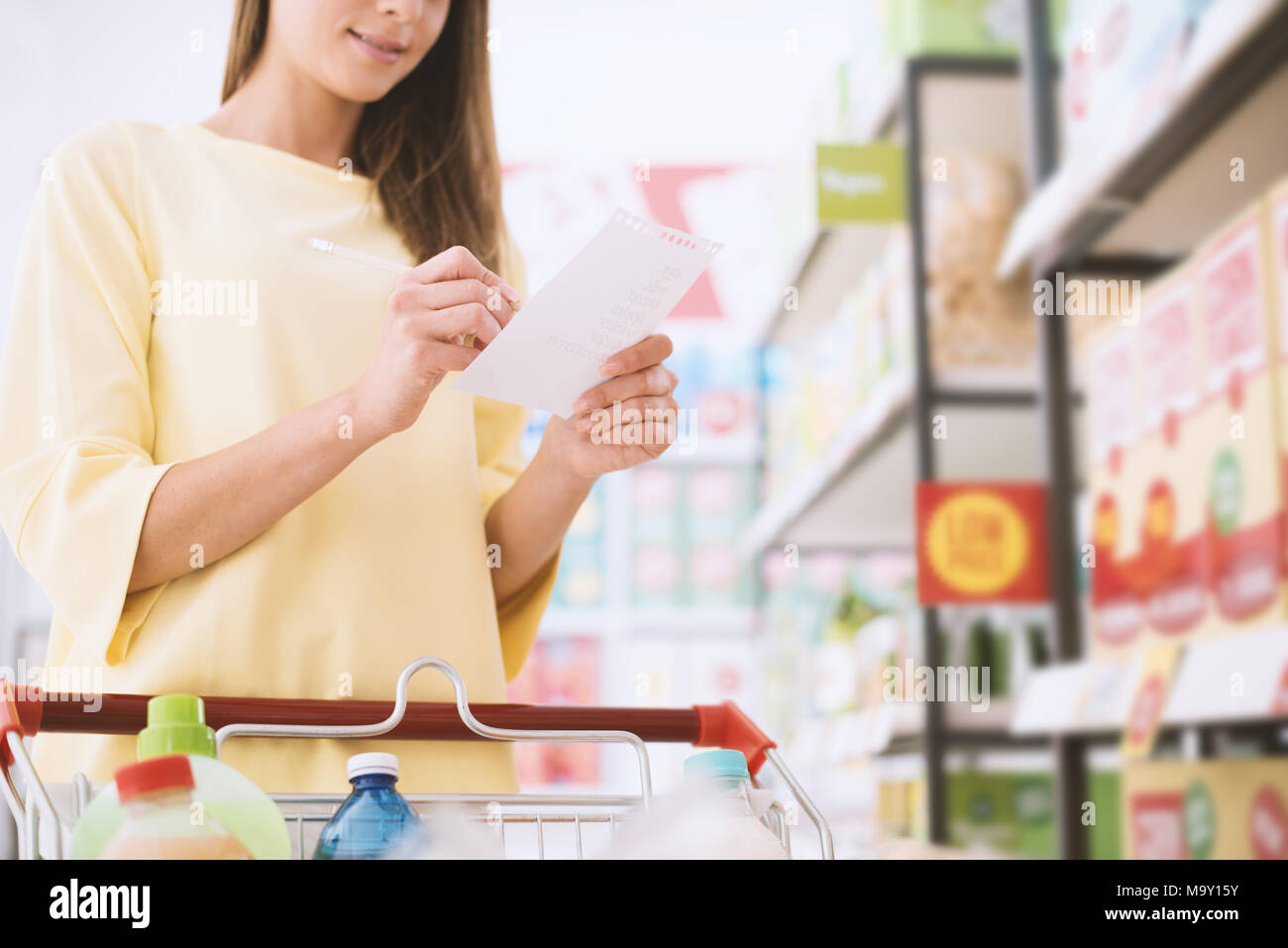 Woman shopping at the grocery store, she is checking items on a list ...