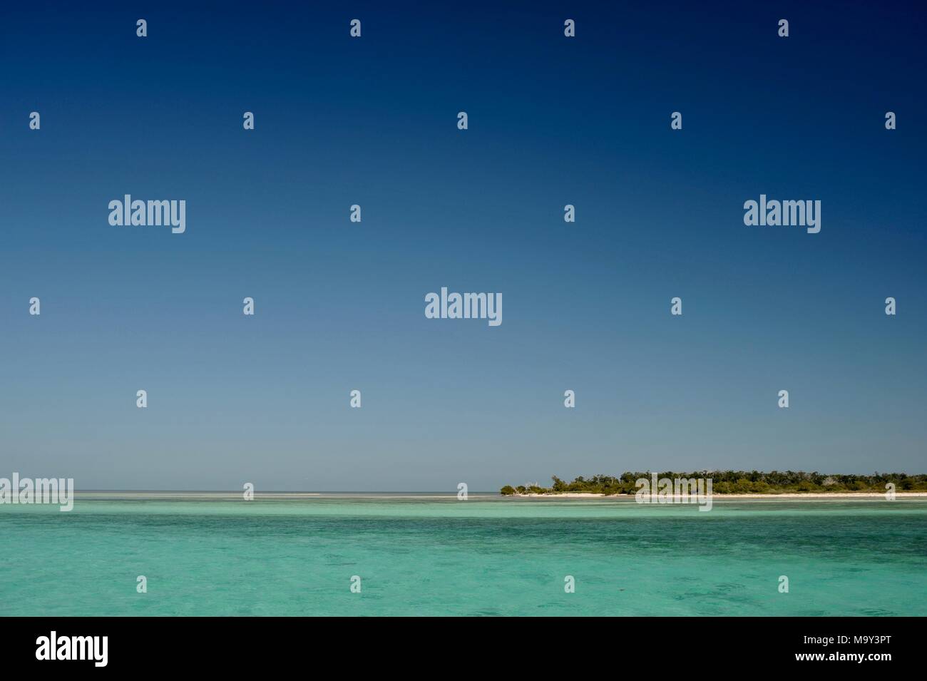 Distant white sandy beach-rimmed island with clear blue sky and ...