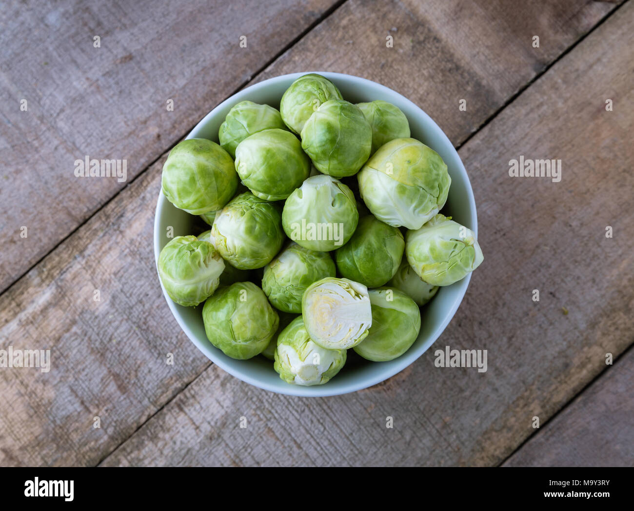 Raw brussels sprouts in white bowl on wooden desk. Top view Stock Photo ...