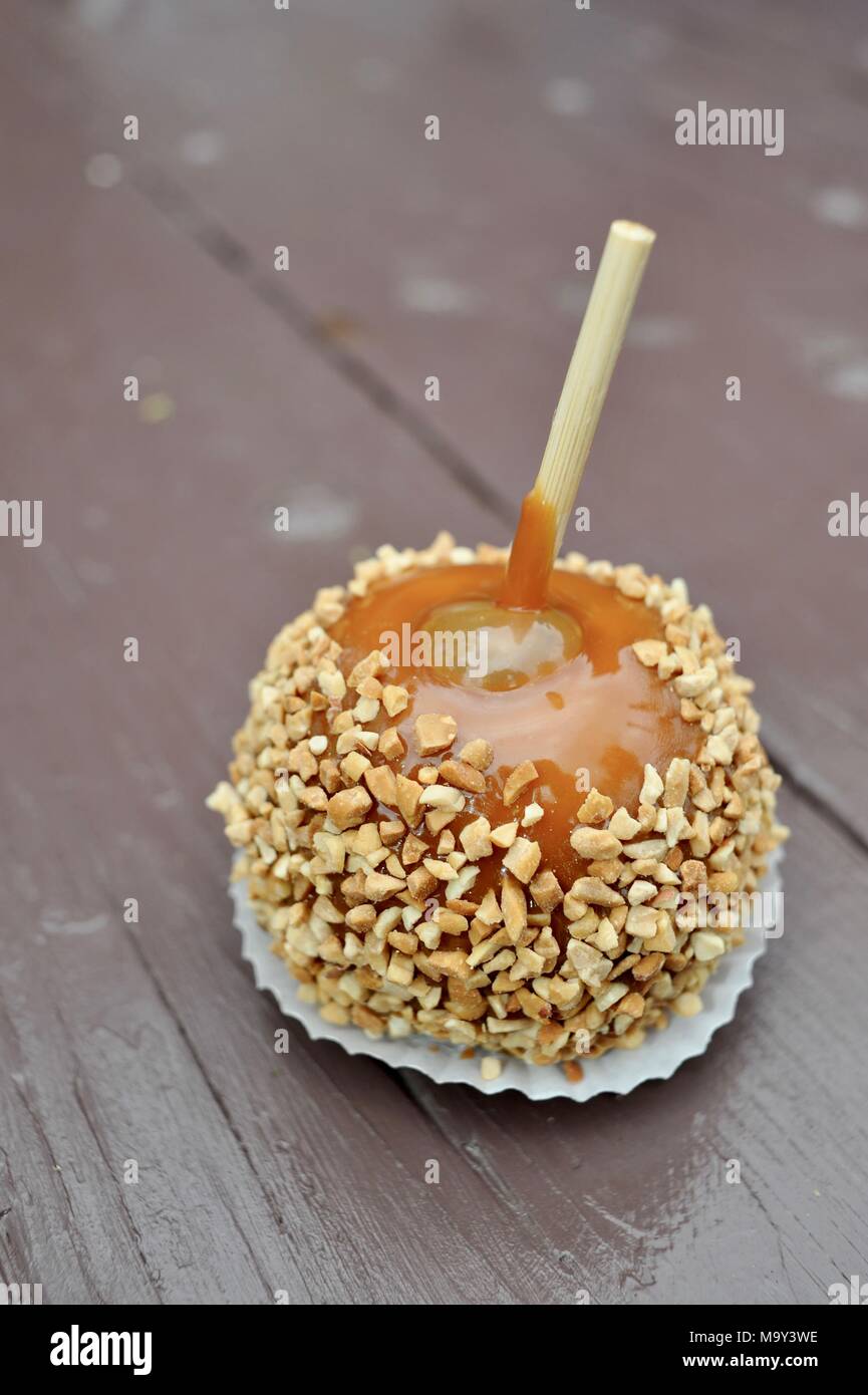 Crushed peanuts on caramel covered large fresh apple on brown wooden ...