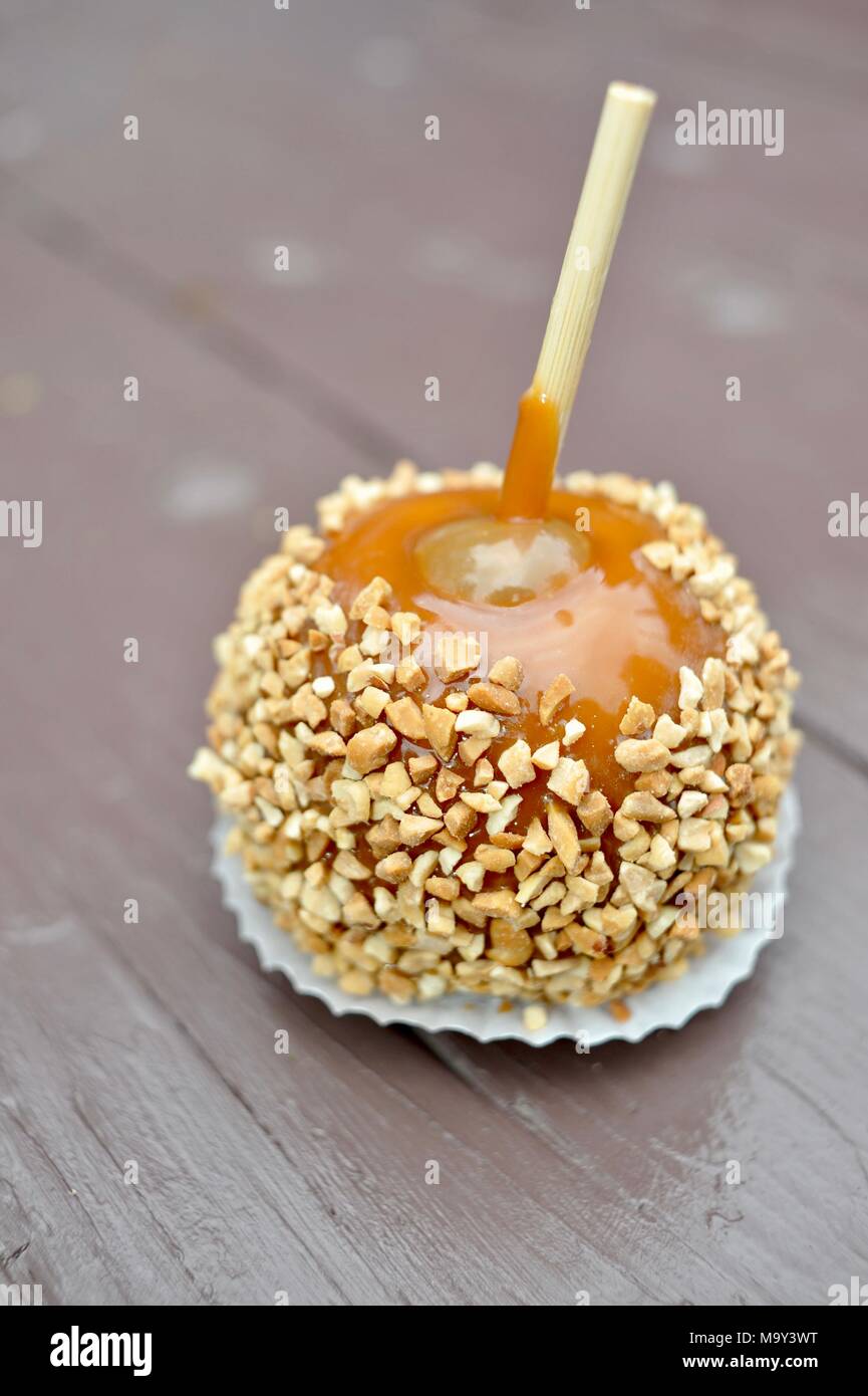 Crushed peanuts on caramel covered large fresh apple on brown wooden ...
