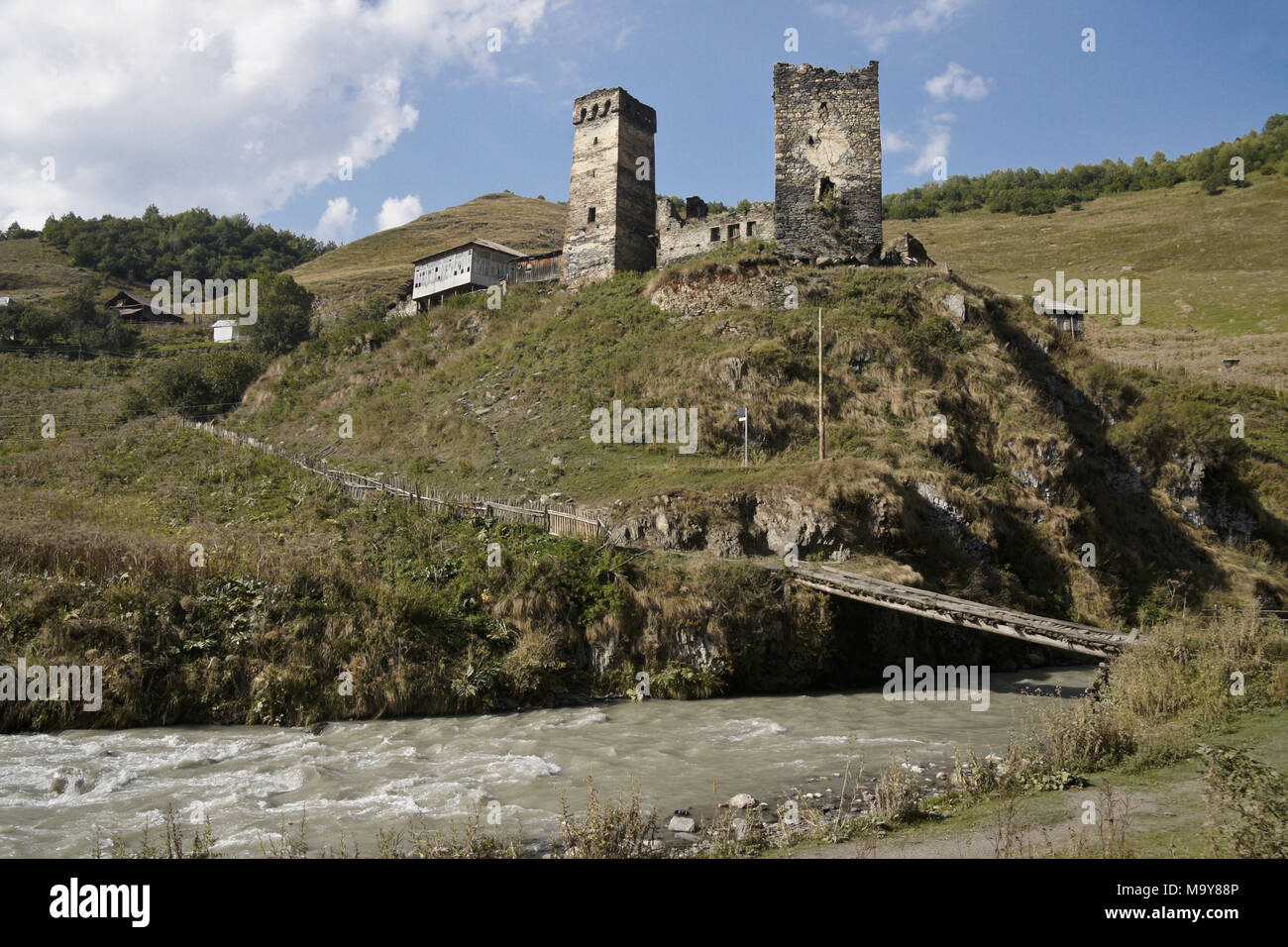 A wood bridge crosses the Inguri (Enguri) River below historic tower ...
