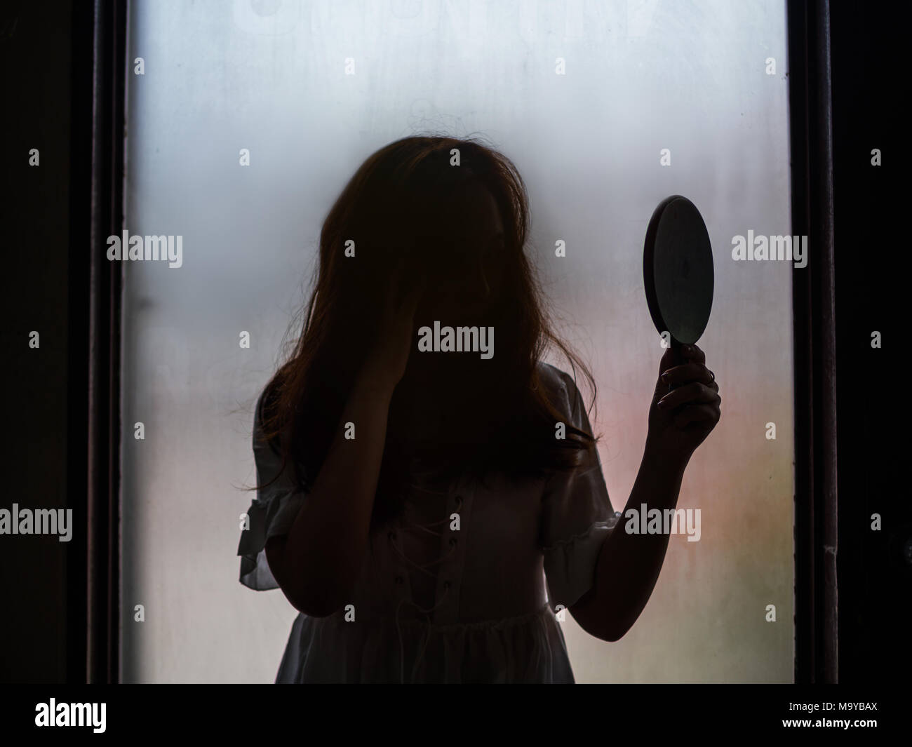Ghost girl holding mirror standing in front of window Stock Photo - Alamy