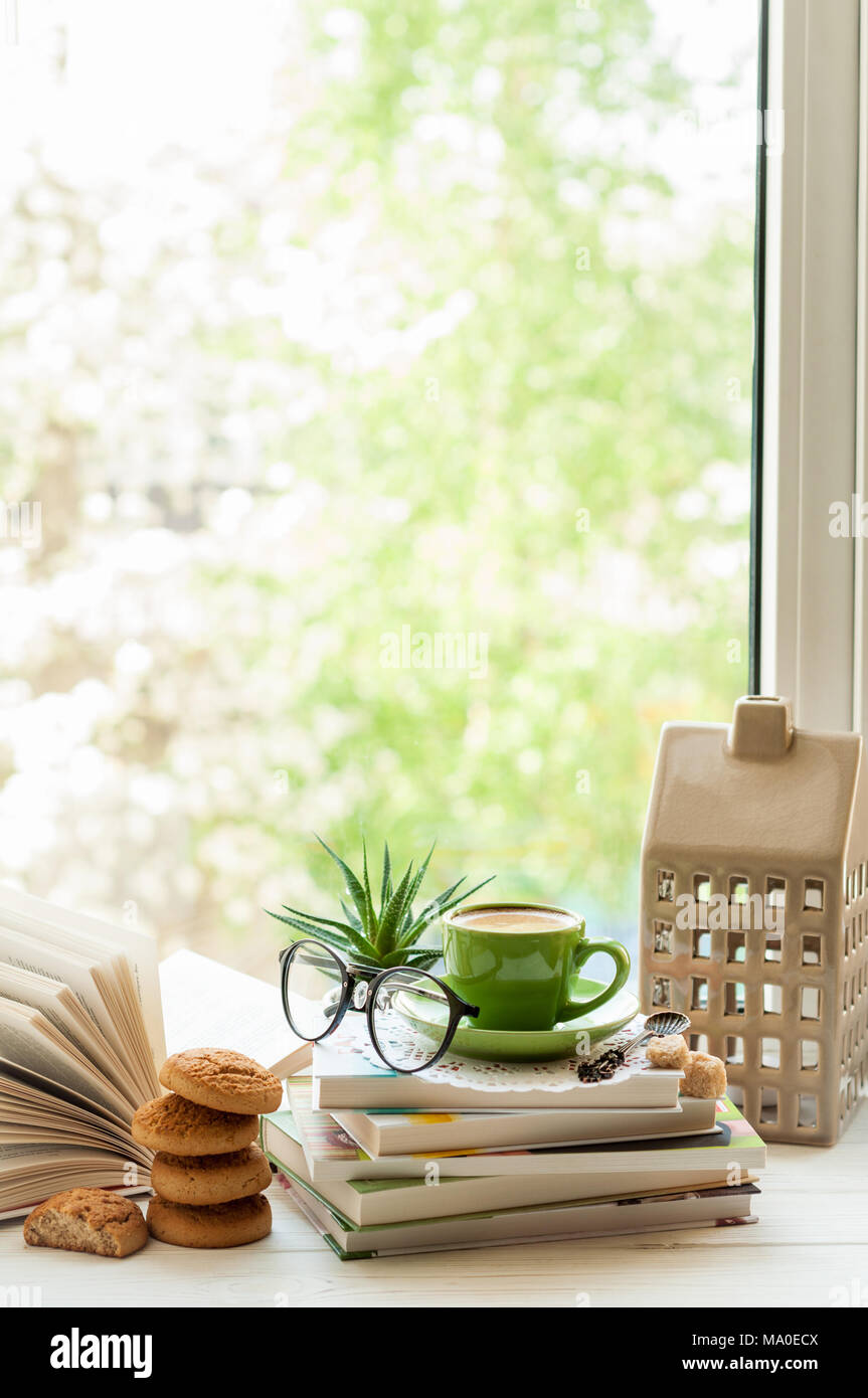 Coffee cup, open book, glasses, cookies and flower on window with bokeh ...