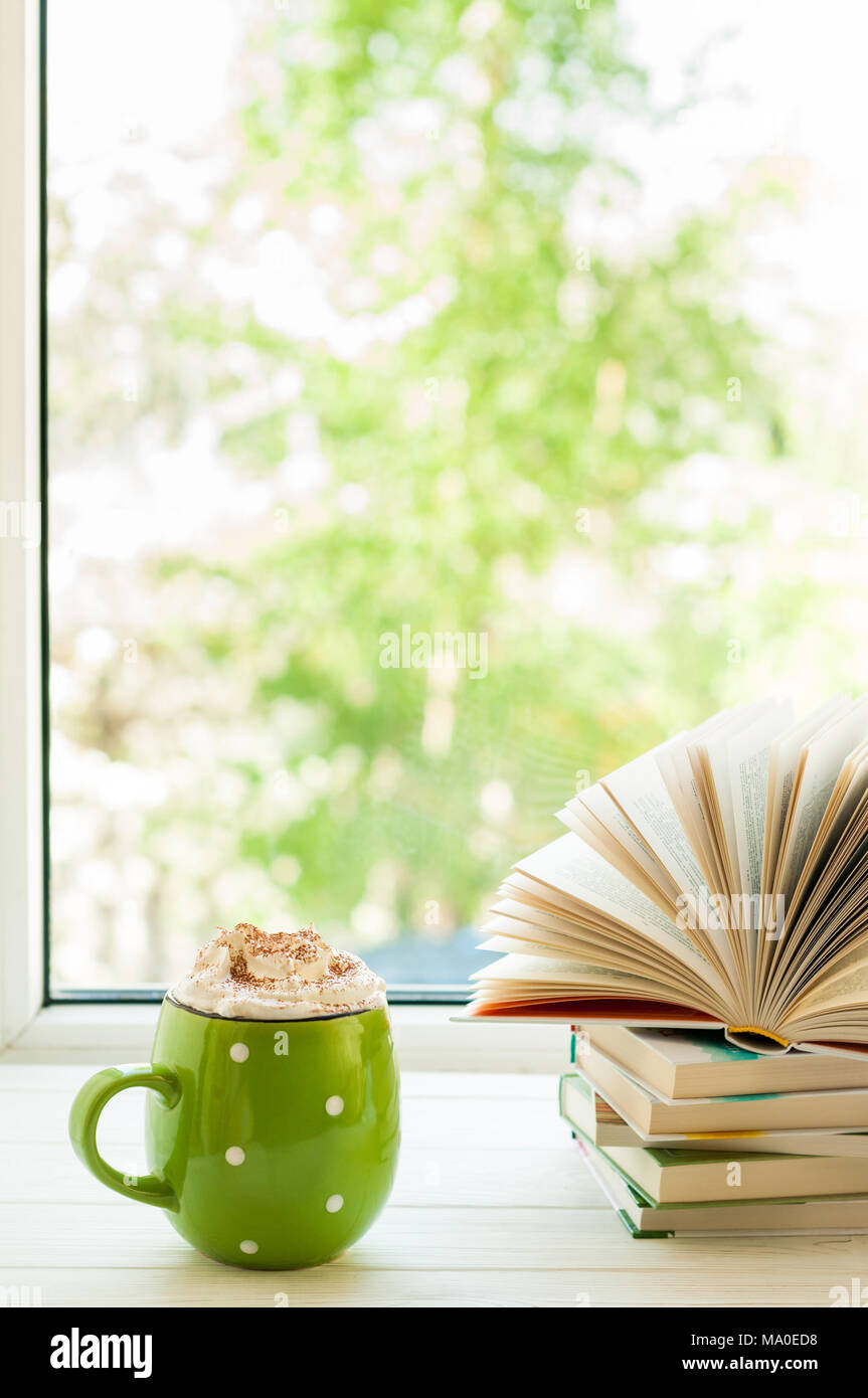 Coffee cup with cream and marshmallows, open book on window with bokeh ...