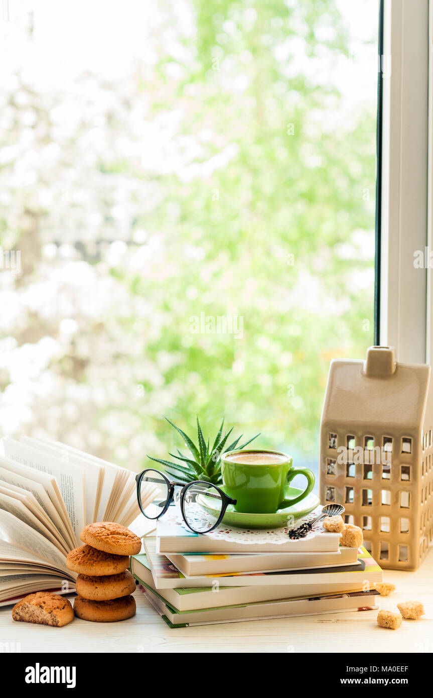 Coffee cup, open book, glasses, cookies and flower on window with bokeh ...