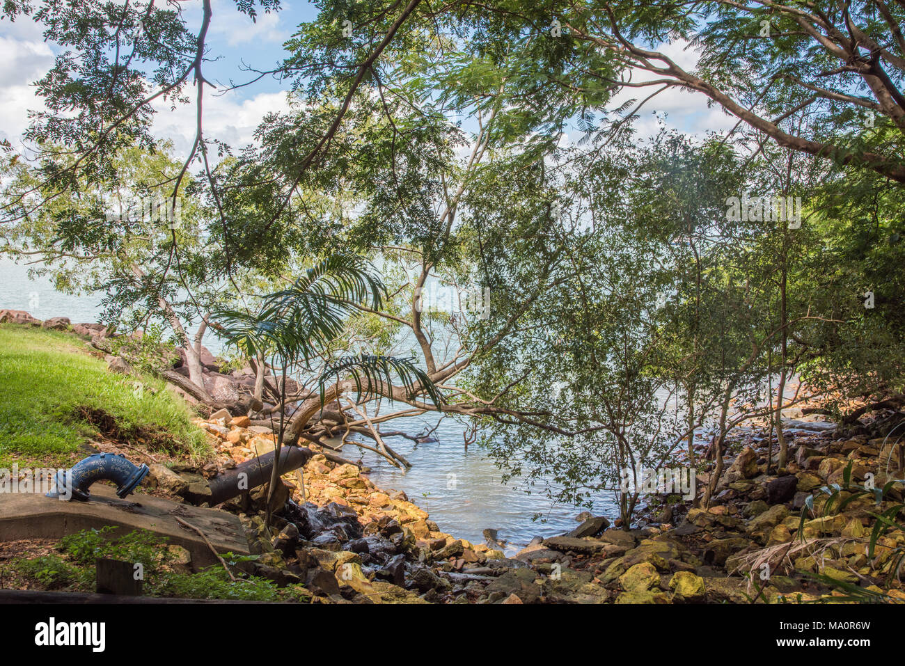 Rocky Timor Sea waterfront with drainage pipe and lush rainforest ...