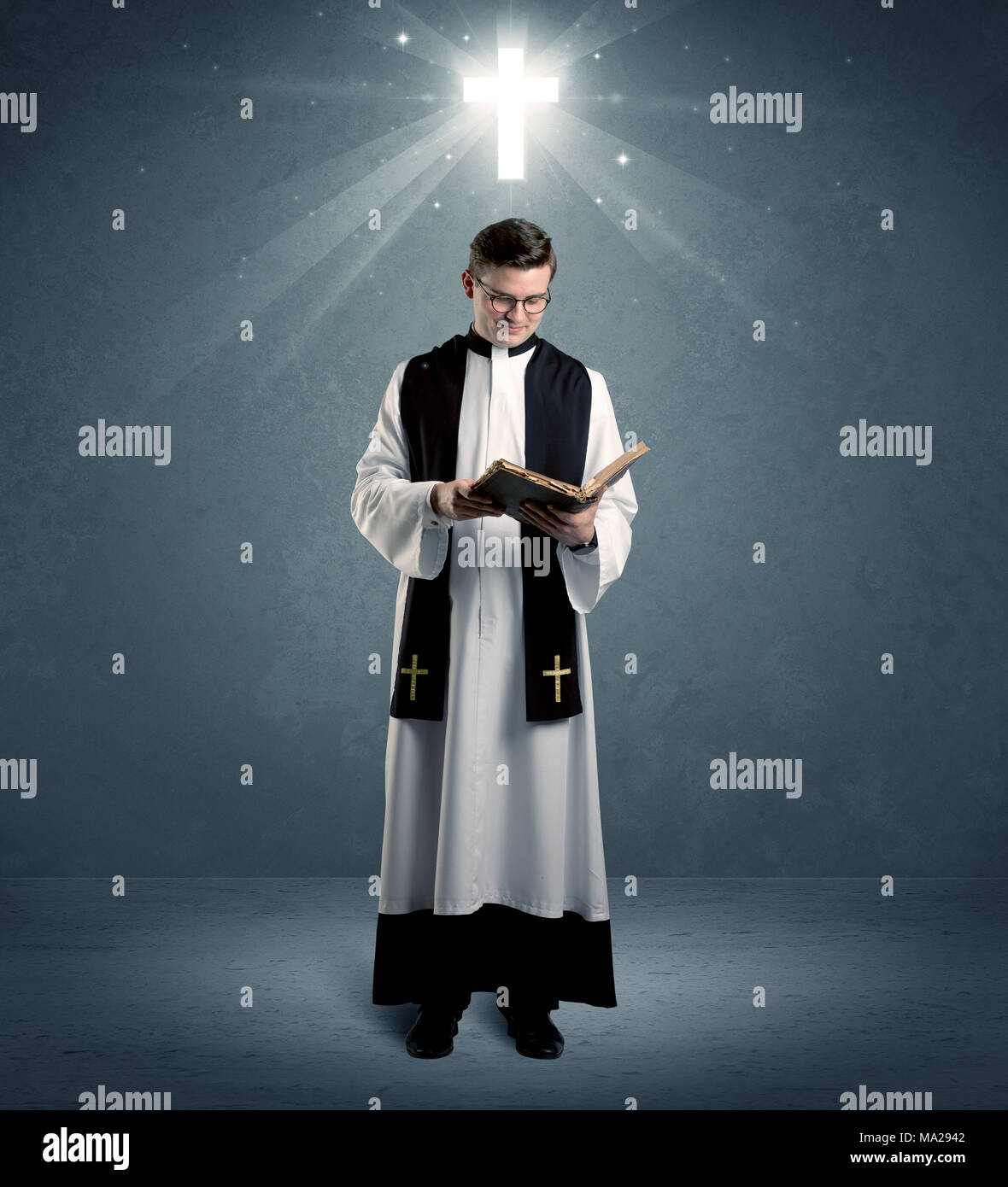 A young caucasian priest with deep faith blessing with the holy bible ...