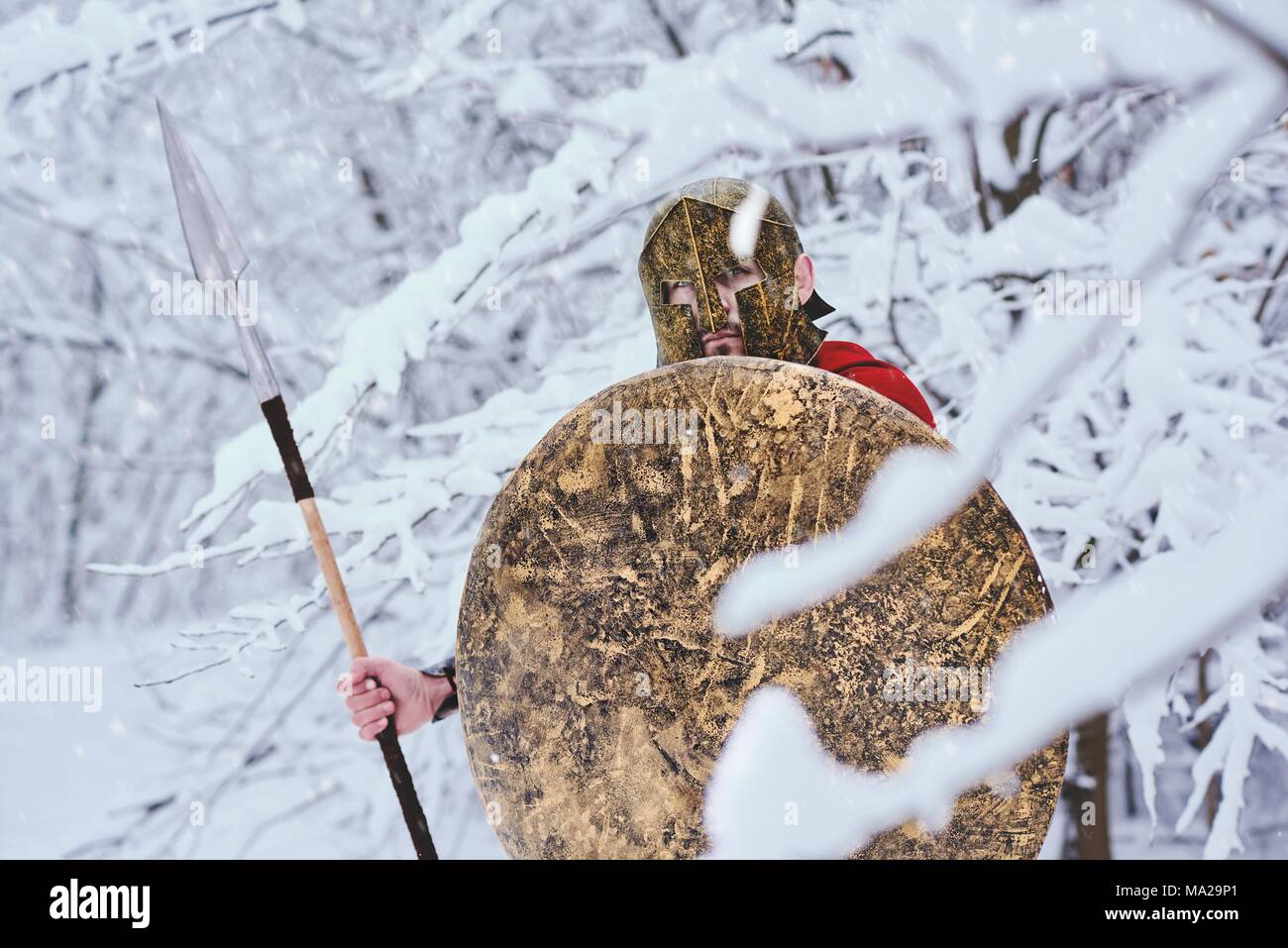 Spartan man took cover under snowy branches in winter forest. He kaaps ...