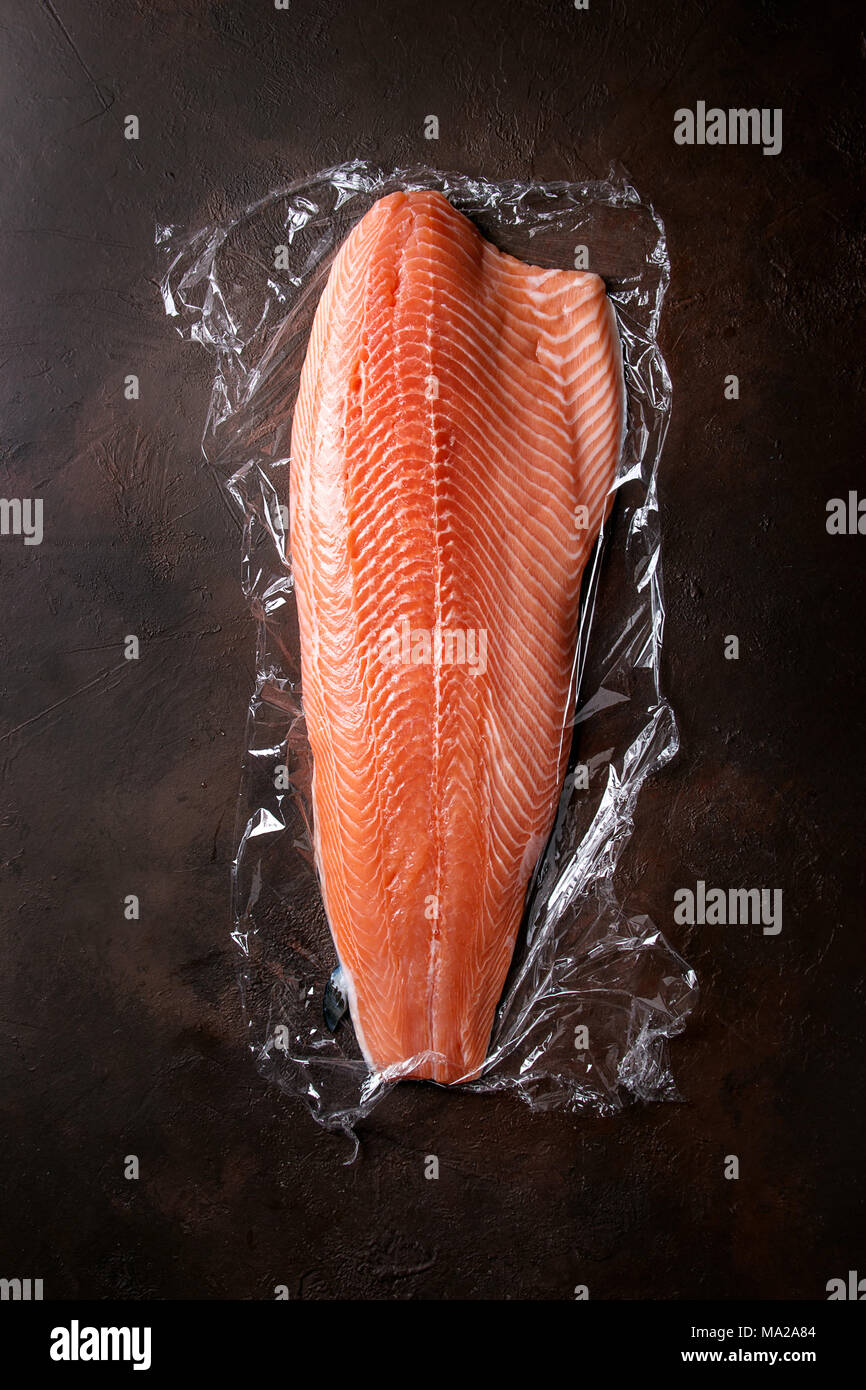 Whole raw uncooked salmon fillet on food film with chef's knife over ...