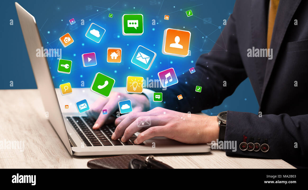 Businessman hand typing on laptop with flying application icons around ...