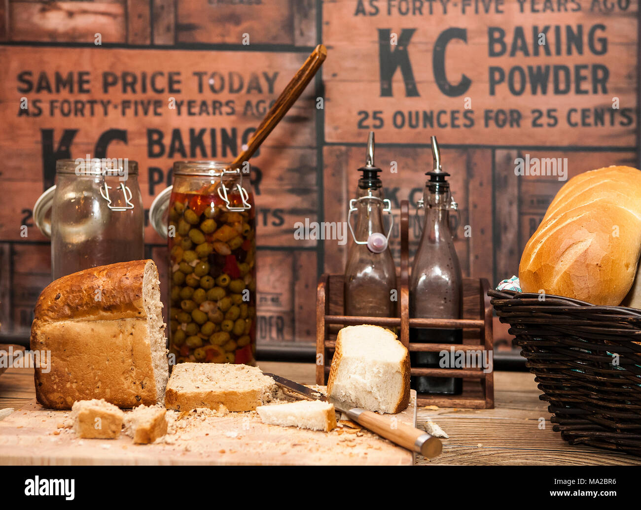 Cut, fresh bread on a breadboard in a restaurant with a jar of olives ...