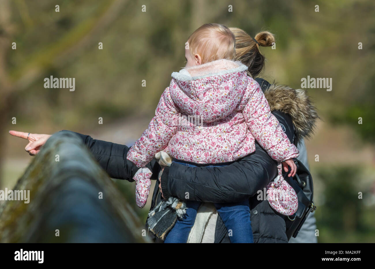 Woman carrying young baby pointing something out on a day out in the UK ...
