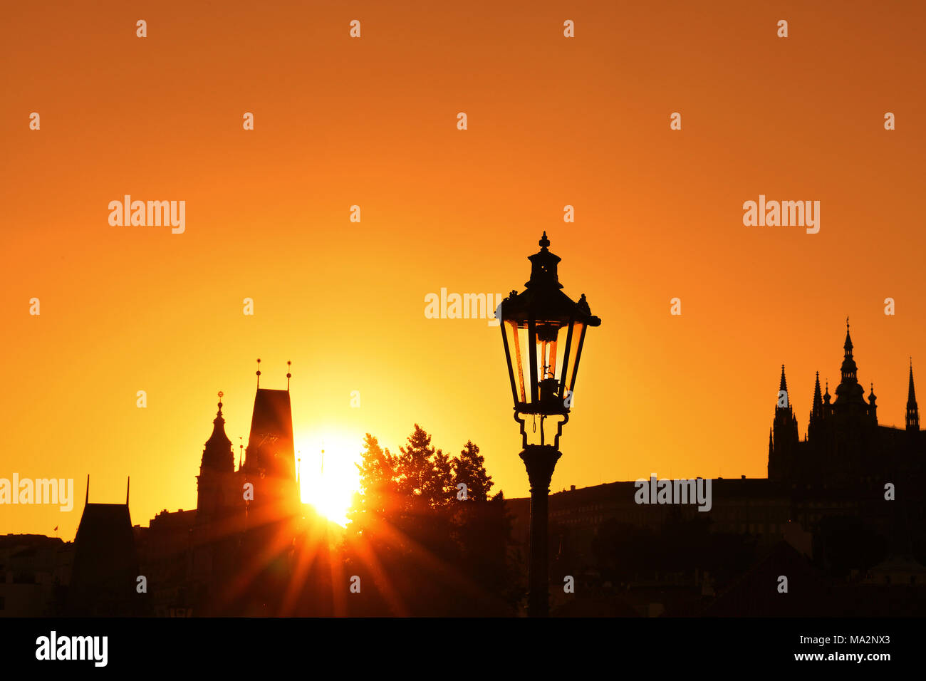 Sunset backlit silhouettes of street lamp post and roofs of cityscape ...