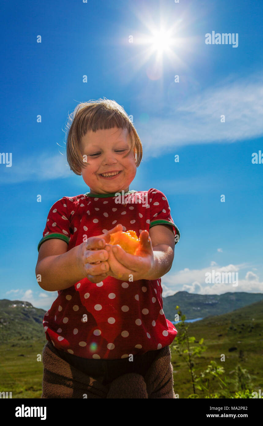 Happy, cute, little boy smiling and holding a sticky peach fruit in his ...
