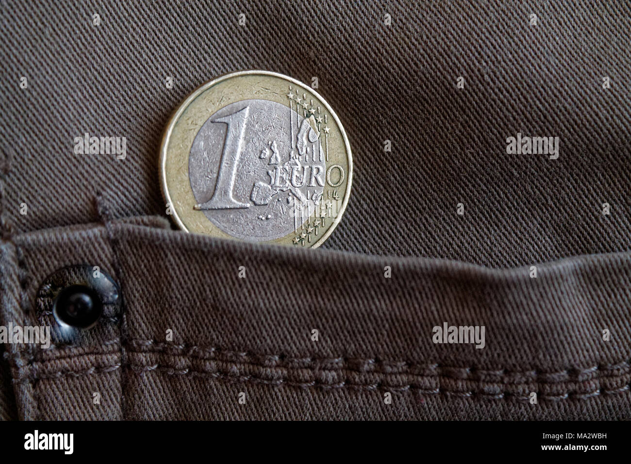 Euro coin with a denomination of one euro in the pocket of brown denim ...