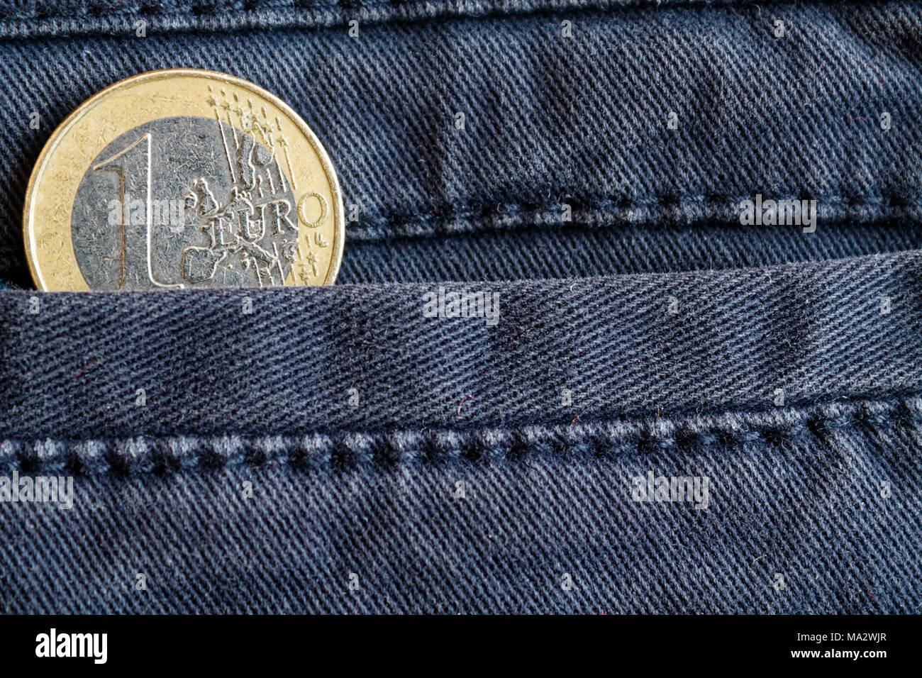 Euro coin with a denomination of one euro in the pocket of blue denim ...