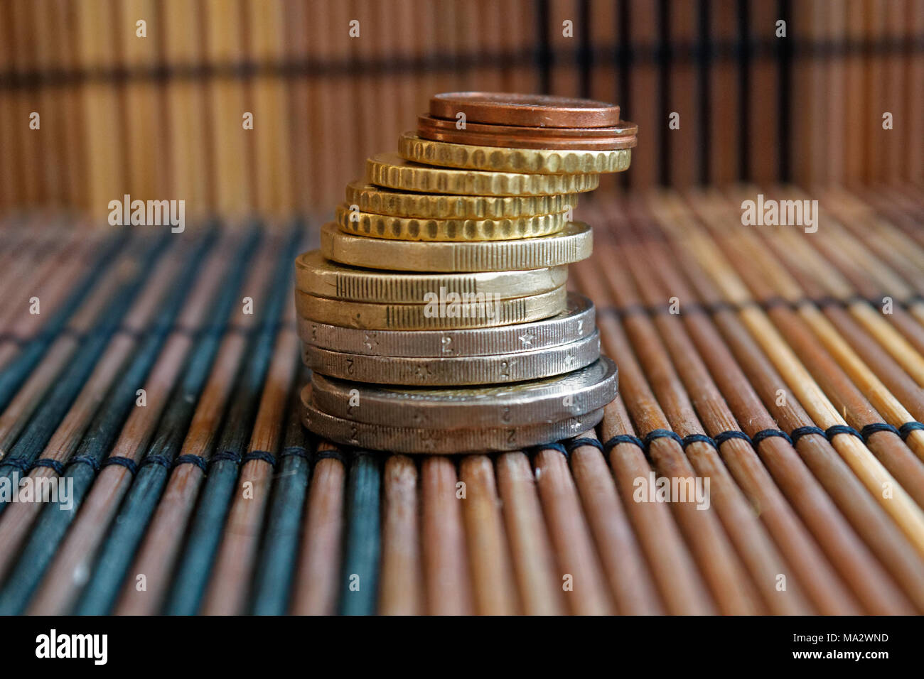 Pile of euro coins, like a tower lies on wooden bamboo table background ...