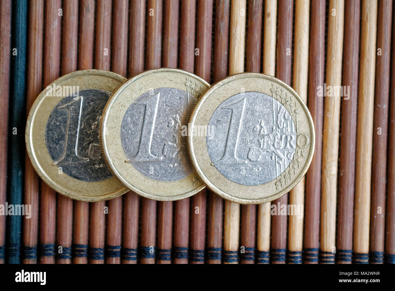 Three euro coins lie on wooden bamboo table in a row Denomination is 1 ...