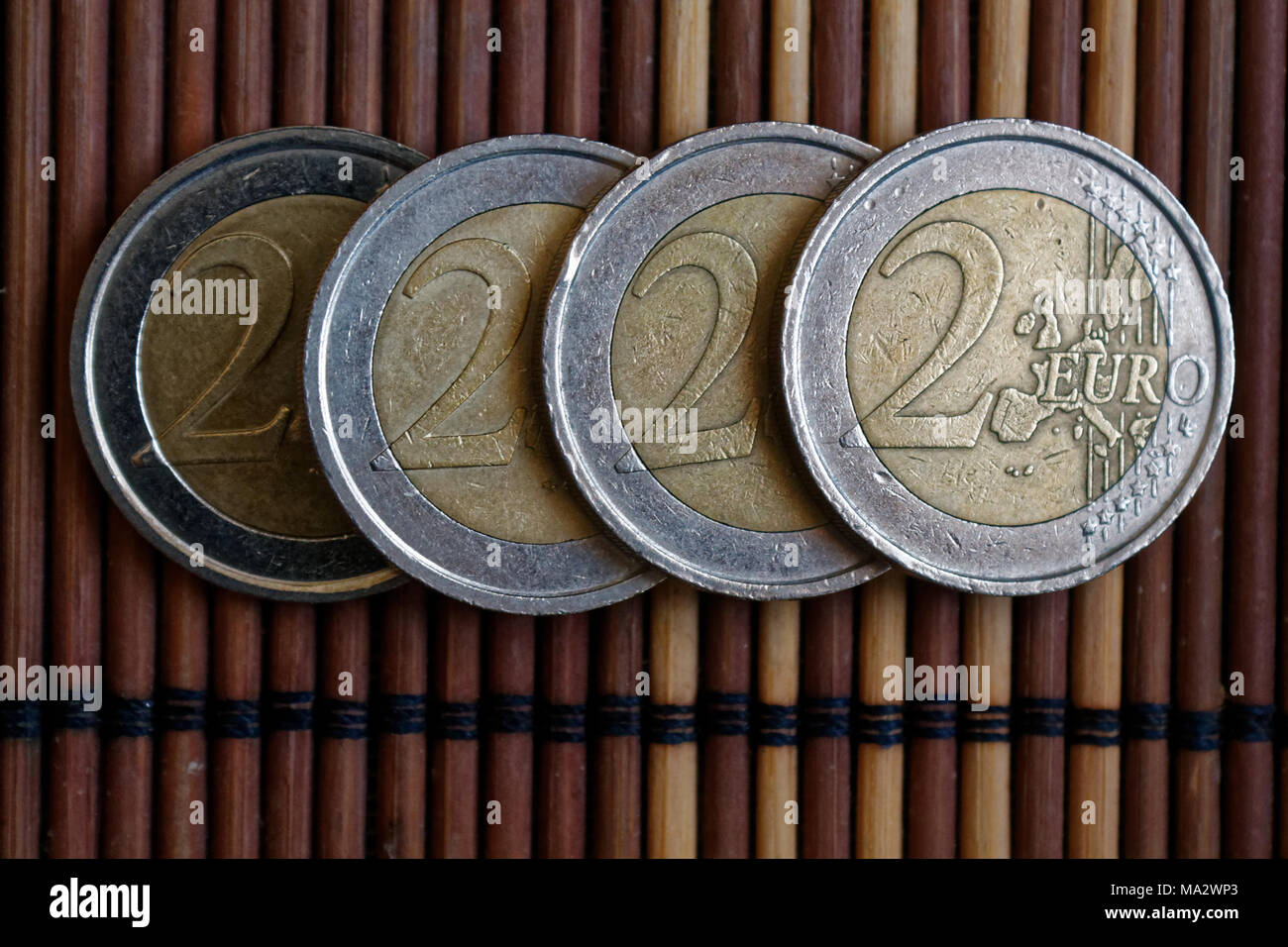 Four euro coins lie on wooden bamboo table in a row Denomination is two ...