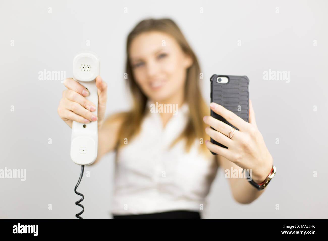 Beautiful girl in a business suit on a white background with two phones ...