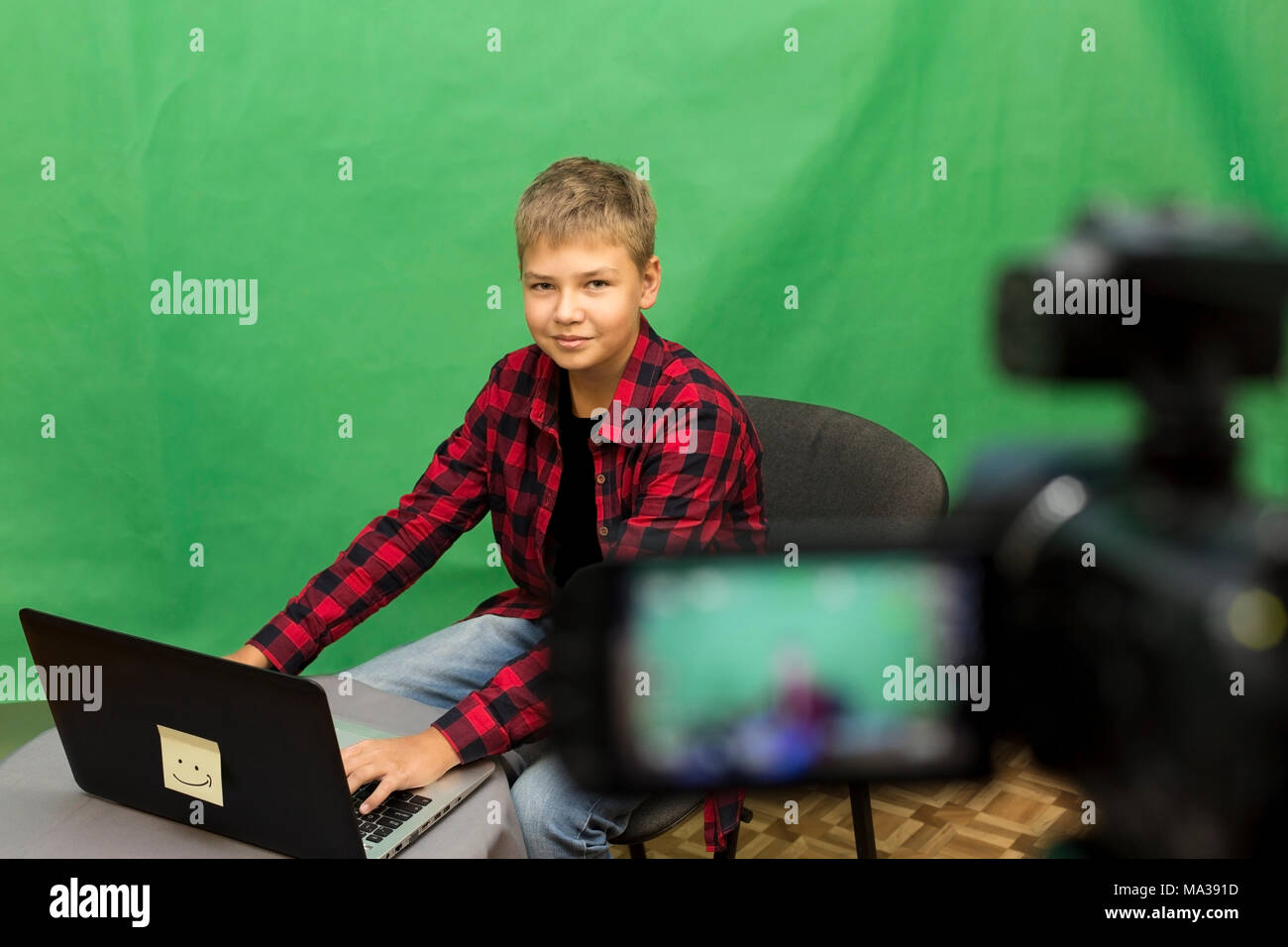 A boy blogger records a video on a green background at home on a video ...