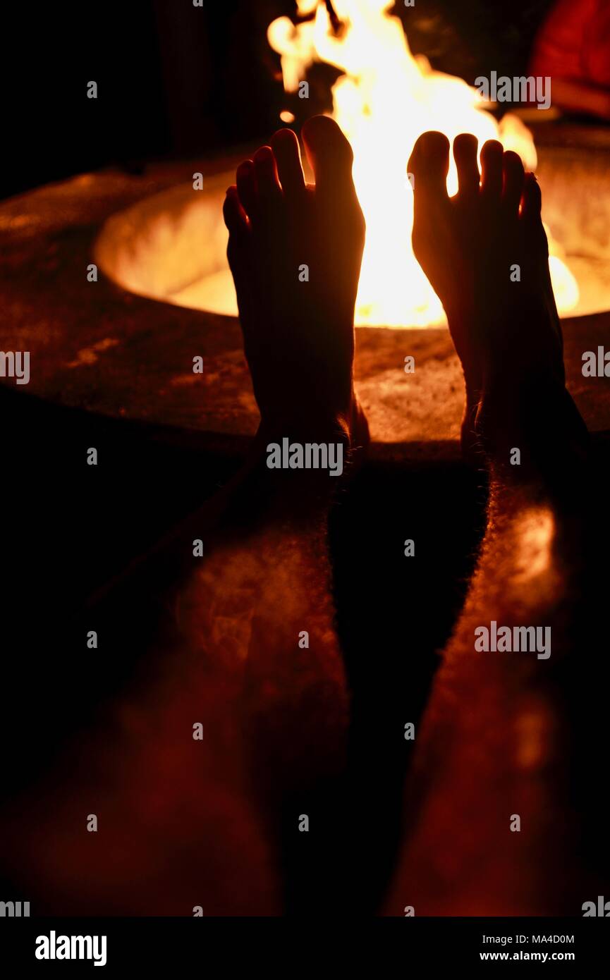 Man resting his bare feet on the cement fire pit ring with flickering ...